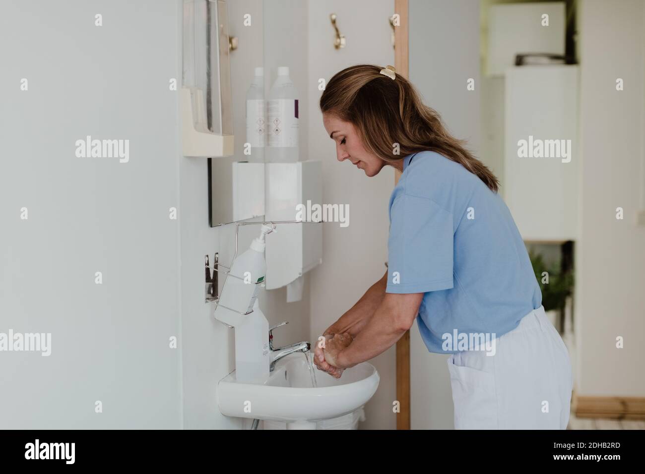 Side view of female doctor washing hands at sink in medical examination ...