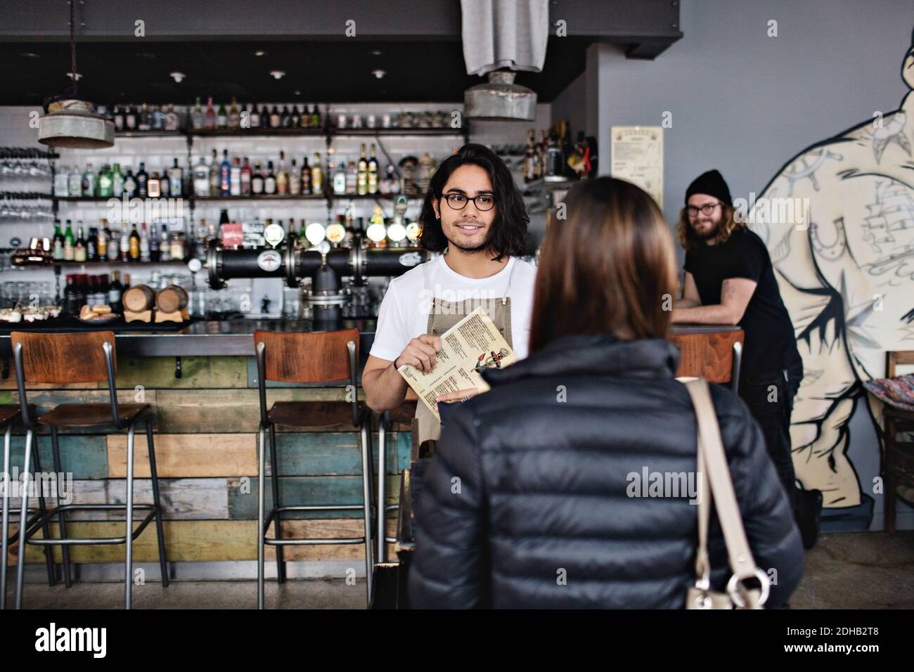 Waiter showing menu to female customer while standing at restaurant ...
