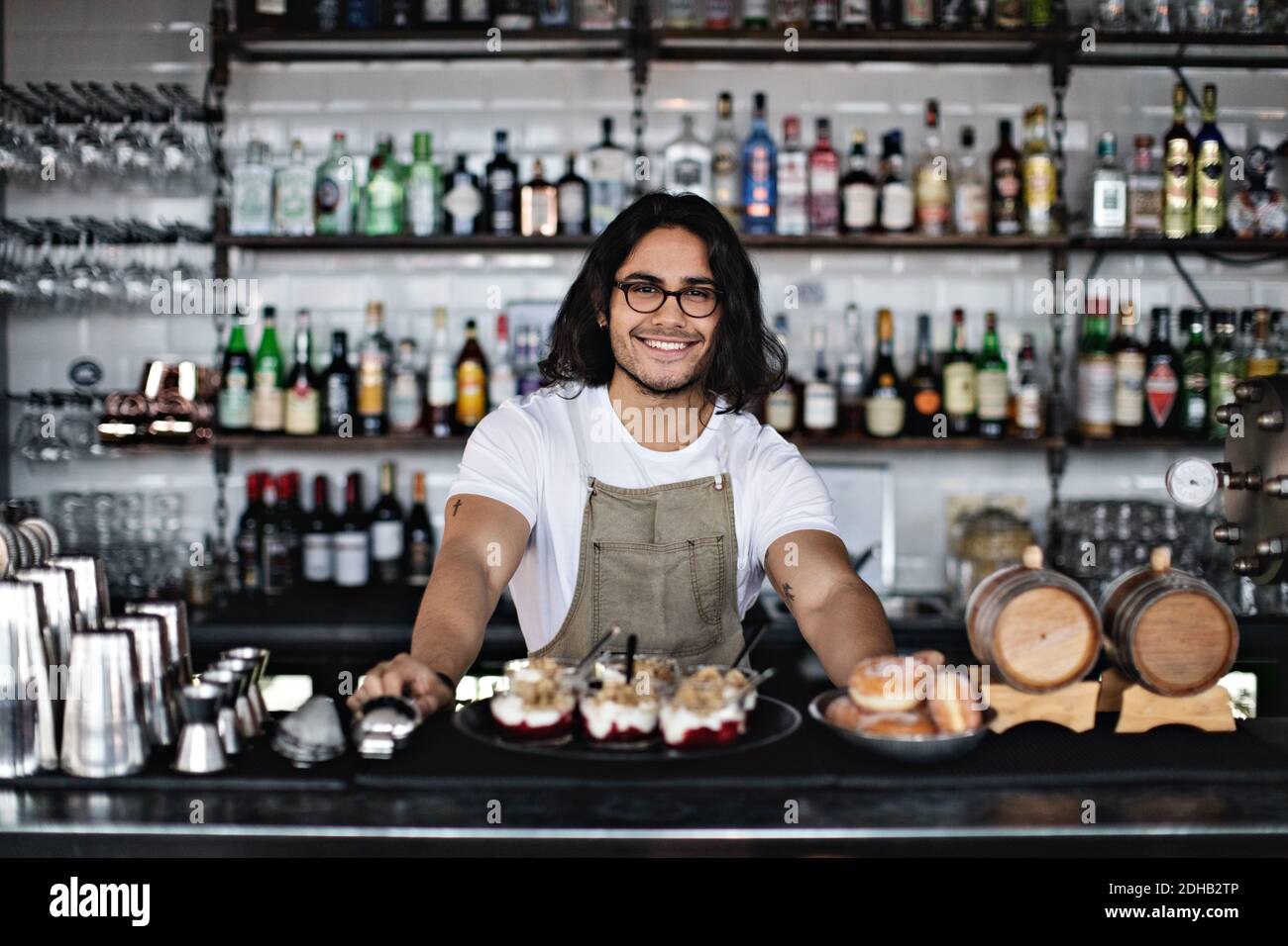Portrait of smiling owner with food standing at counter in restaurant ...