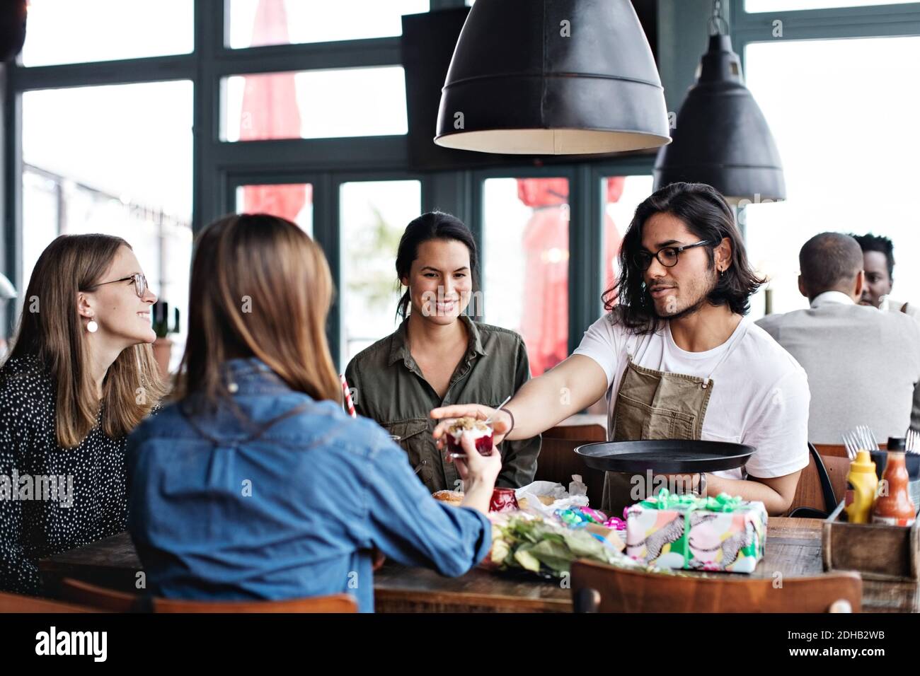 Waiter serving drinks to smiling young female friends sitting at dining ...