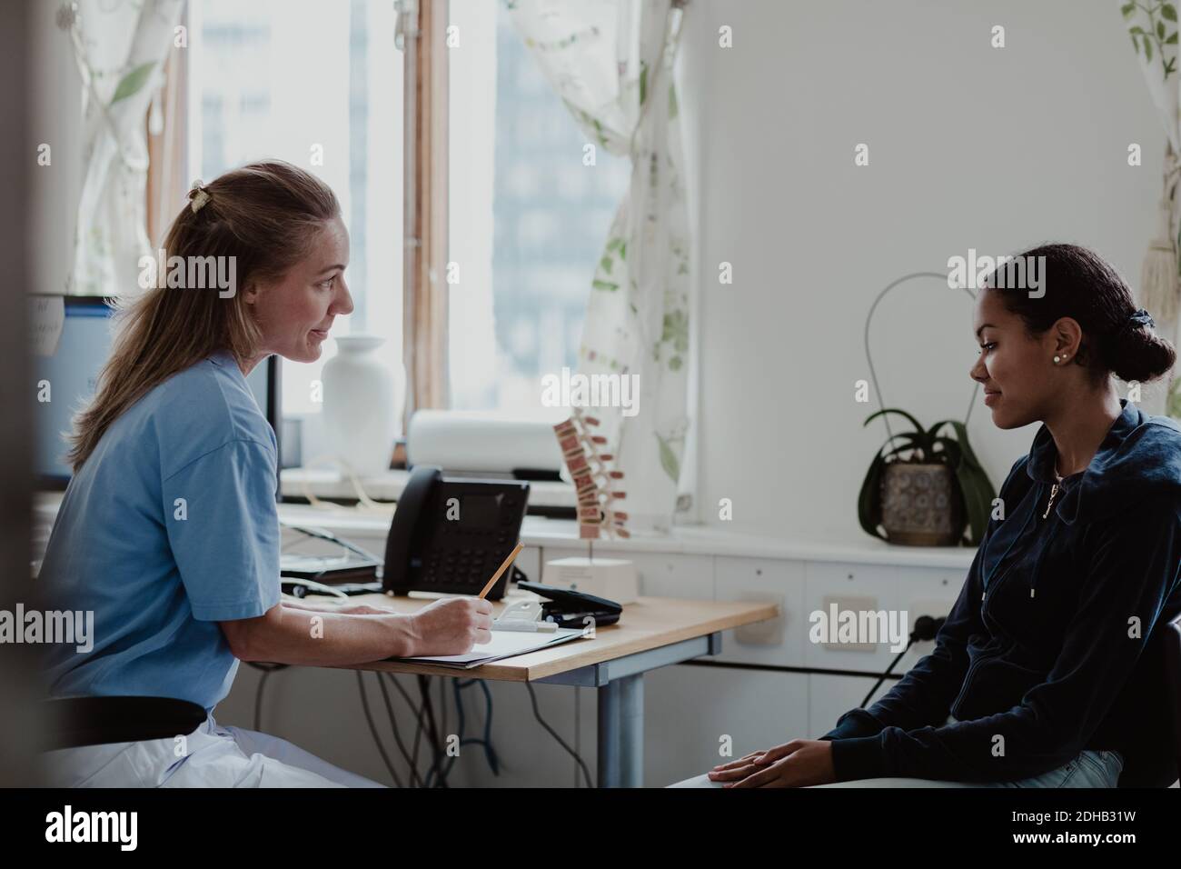 Mature nurse explaining to female patient while sitting at doctor's ...