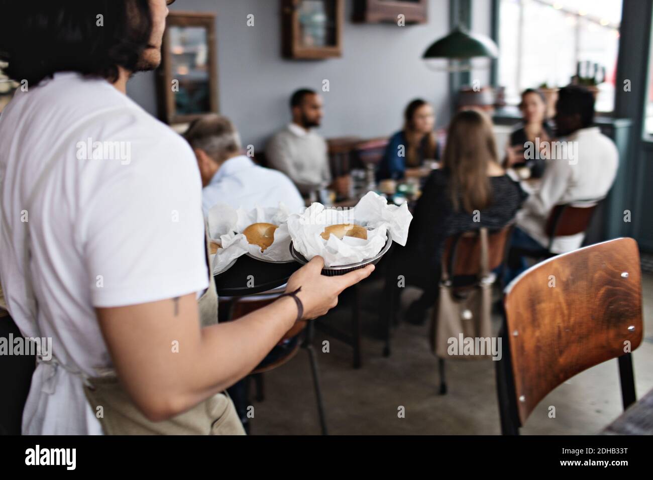 Young waiter serving burgers while walking by customers in restaurant ...