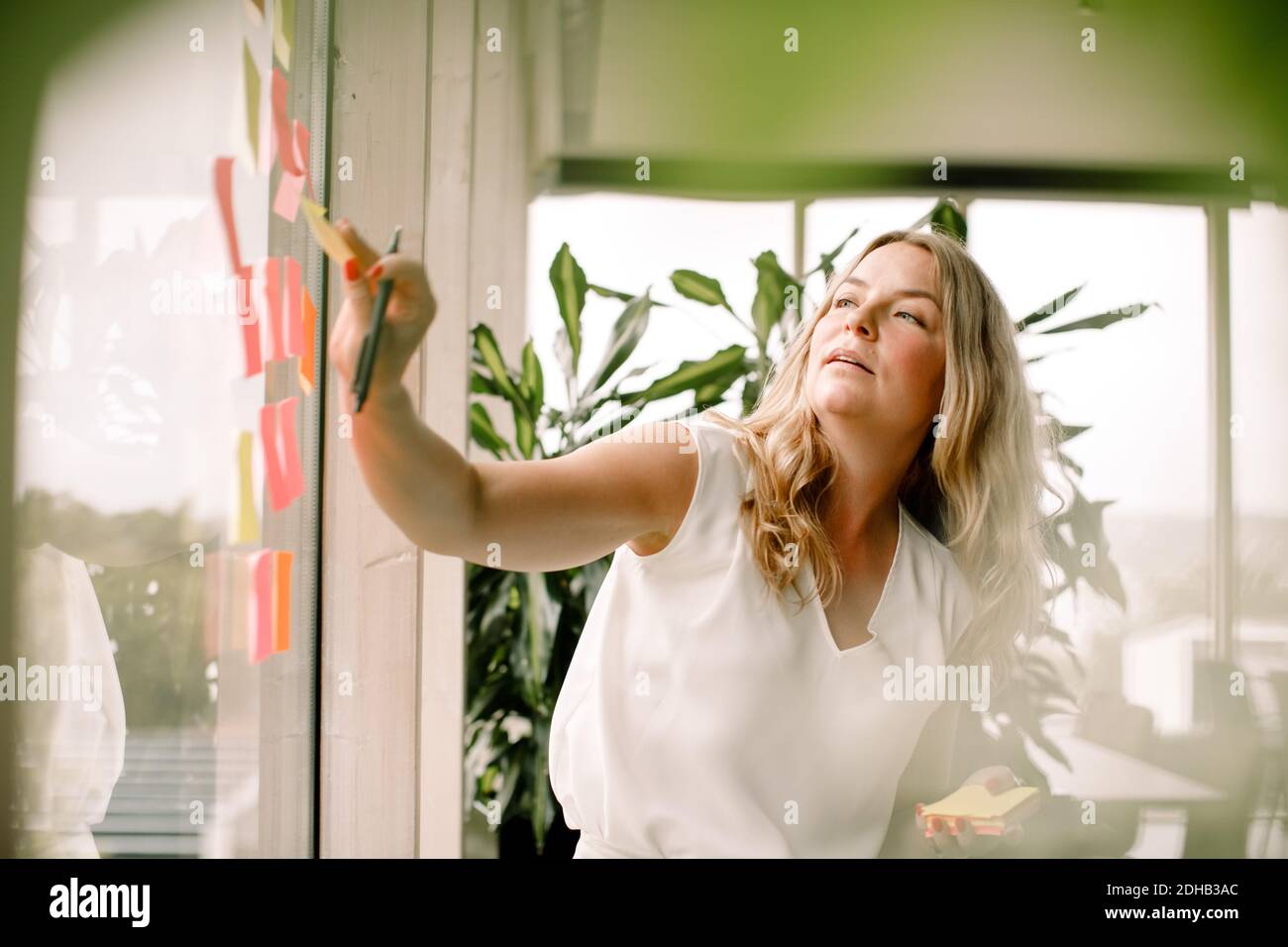 Businesswoman sticking adhesive note on glass window at convention ...