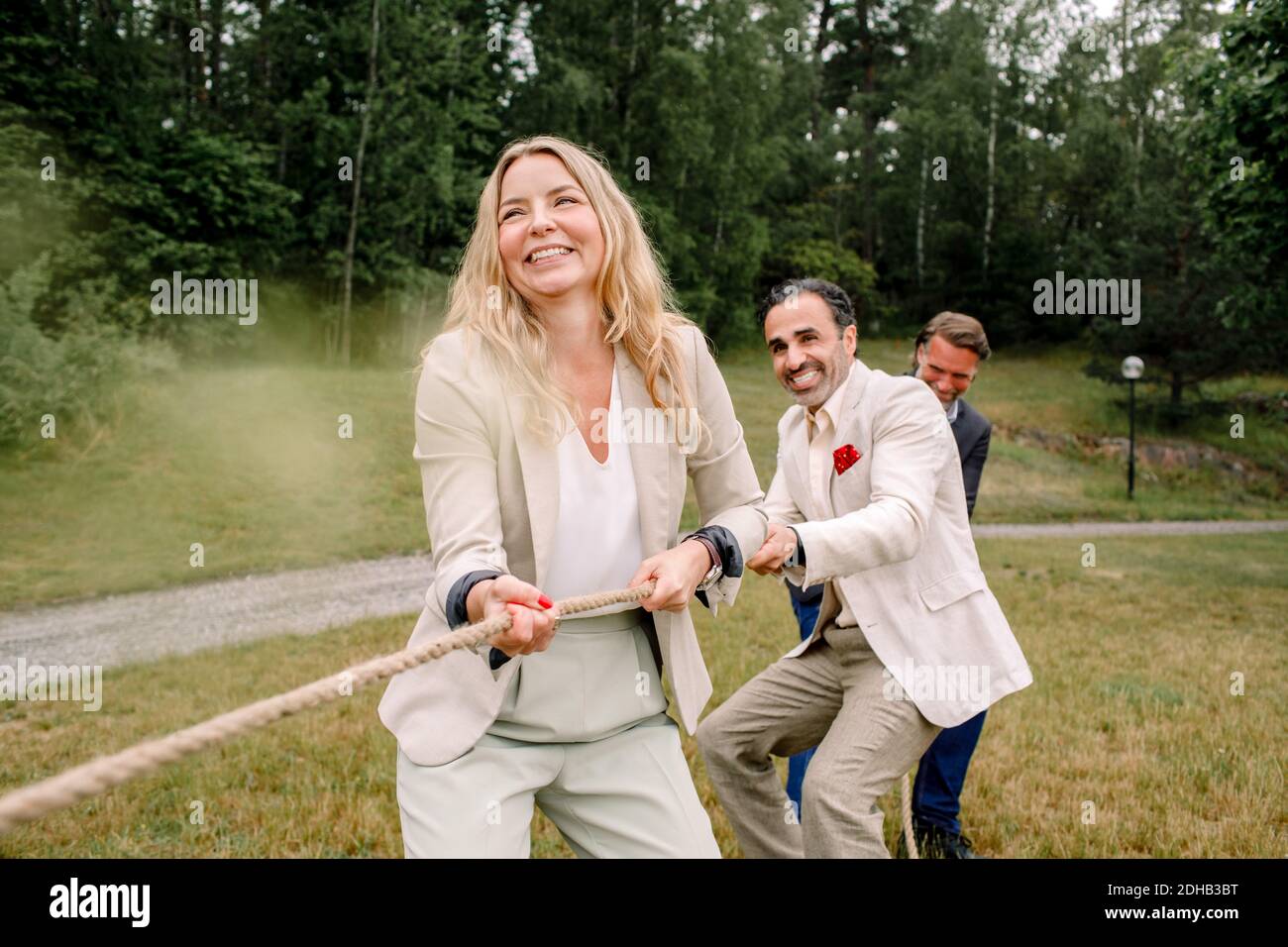 Smiling male and female colleagues pulling rope while playing tug-of ...