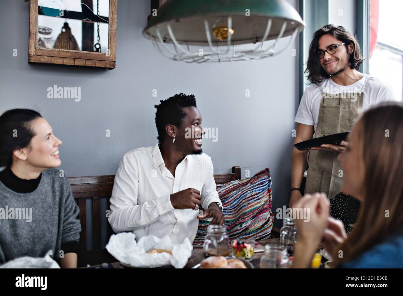 Happy friends looking at young waiter while enjoying brunch in ...