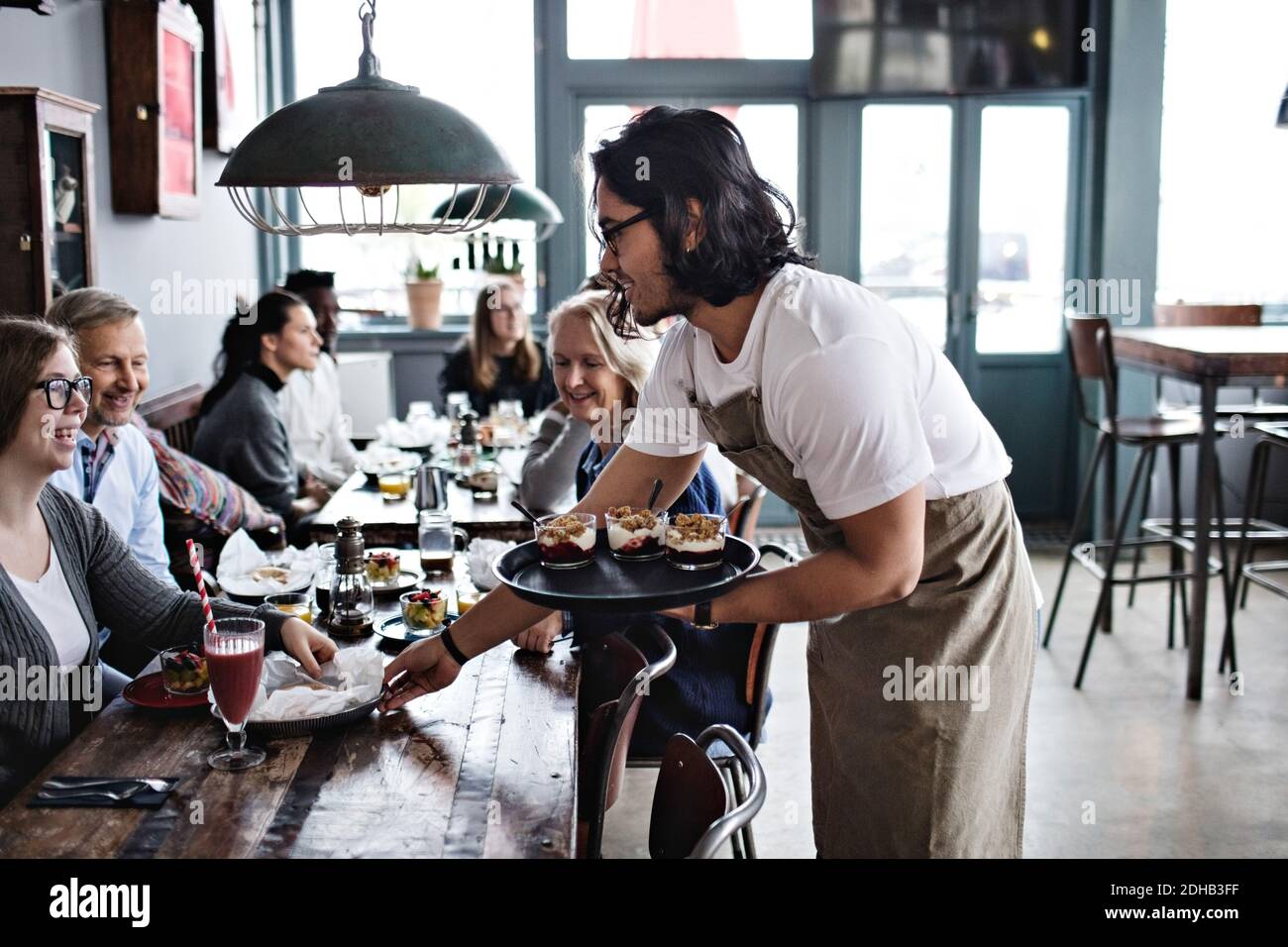 Waiter serving food to smiling customers at restaurant Stock Photo - Alamy