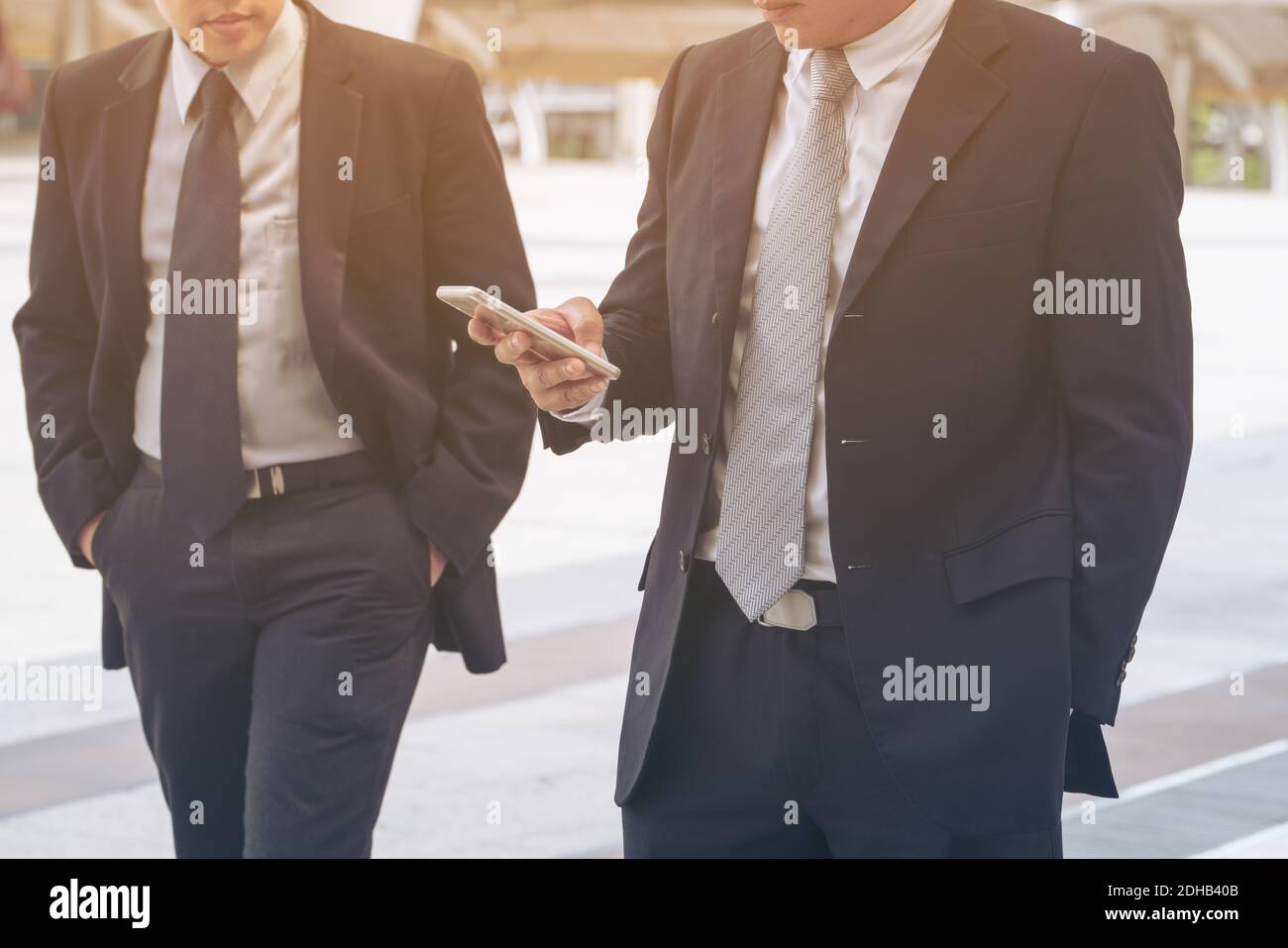 Two business people walking while using mobile phone Stock Photo - Alamy