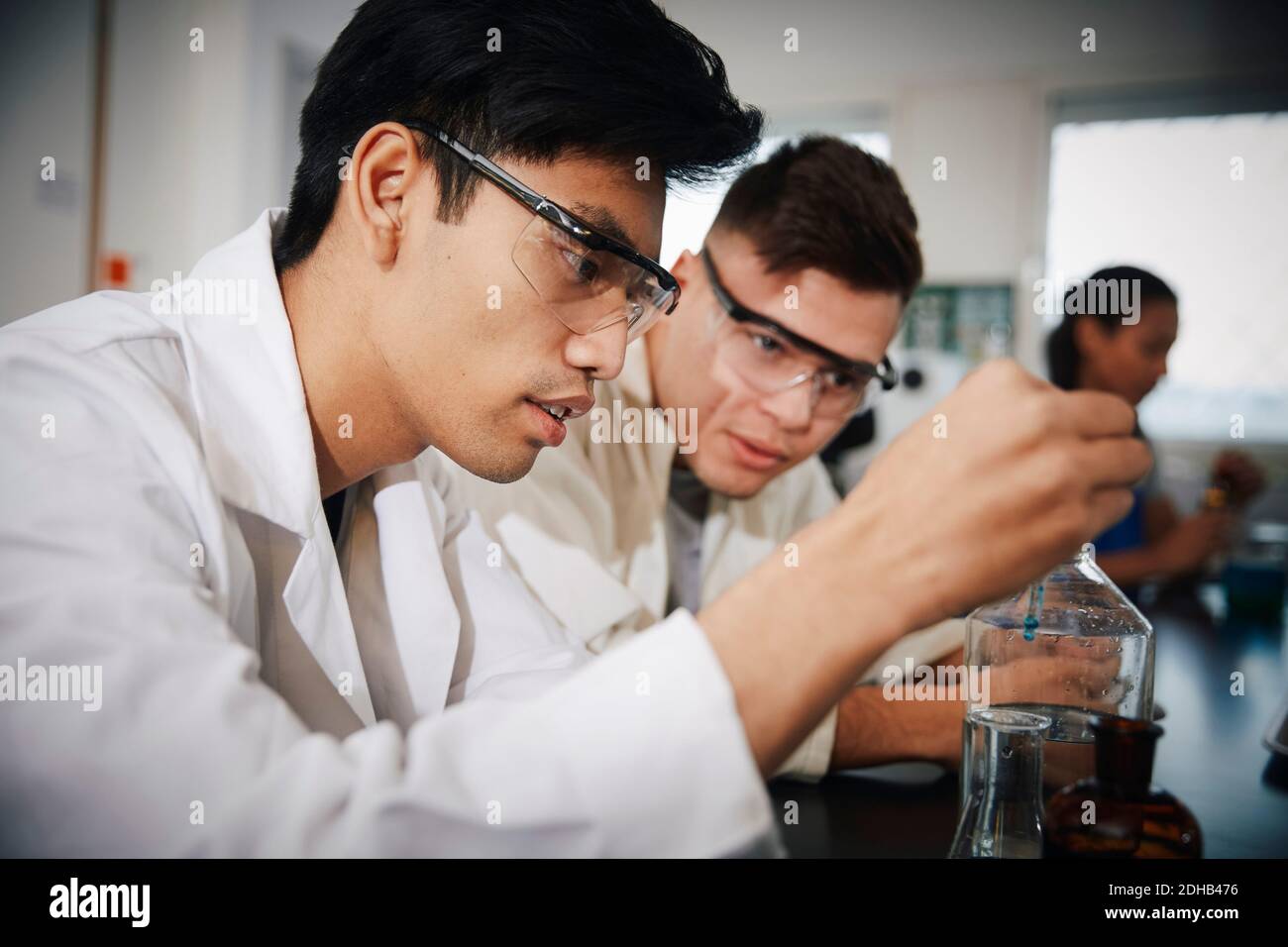 Young male students mixing solutions in glassware at chemistry ...