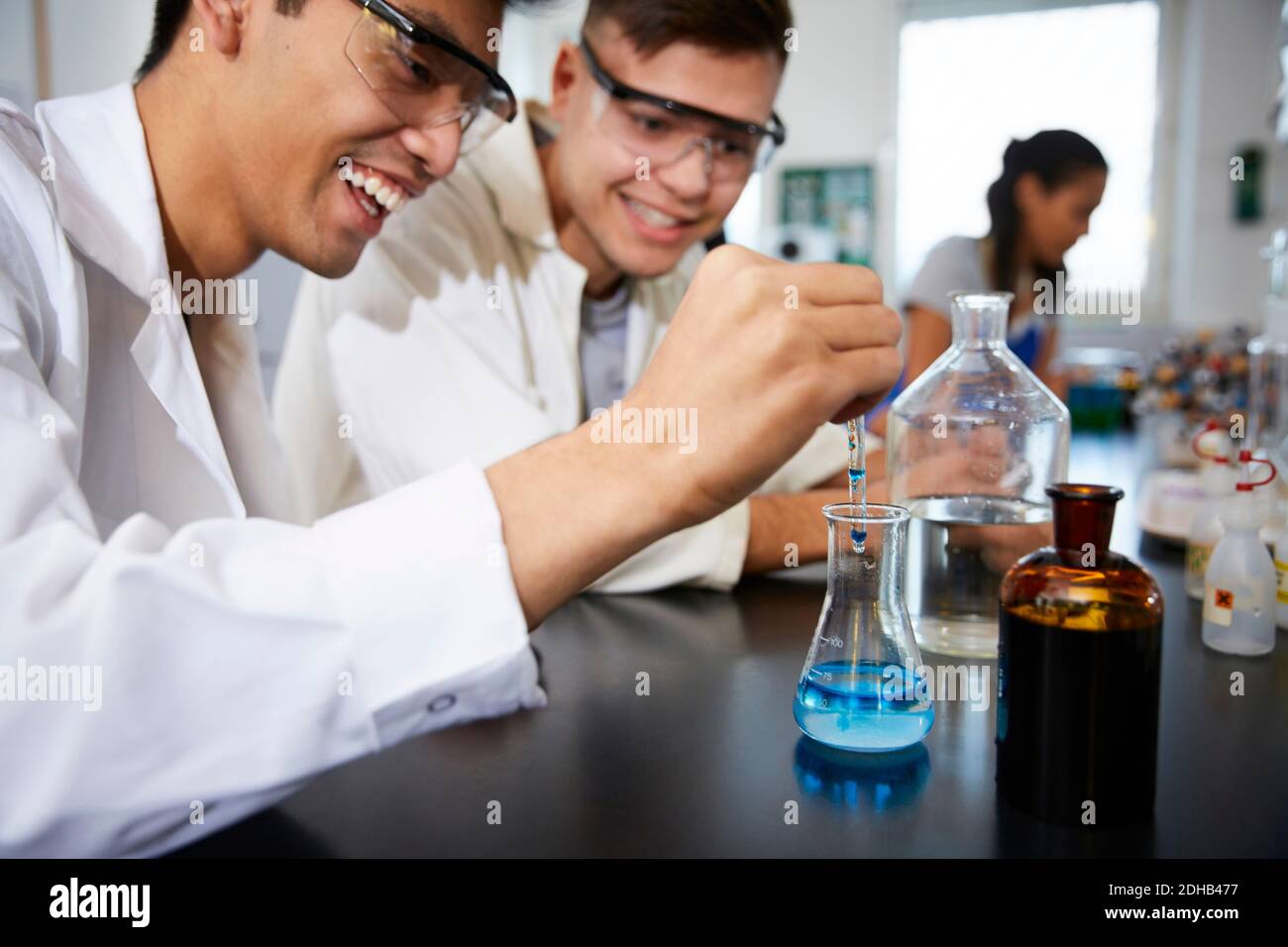 Smiling young male students mixing solutions in glassware at chemistry ...