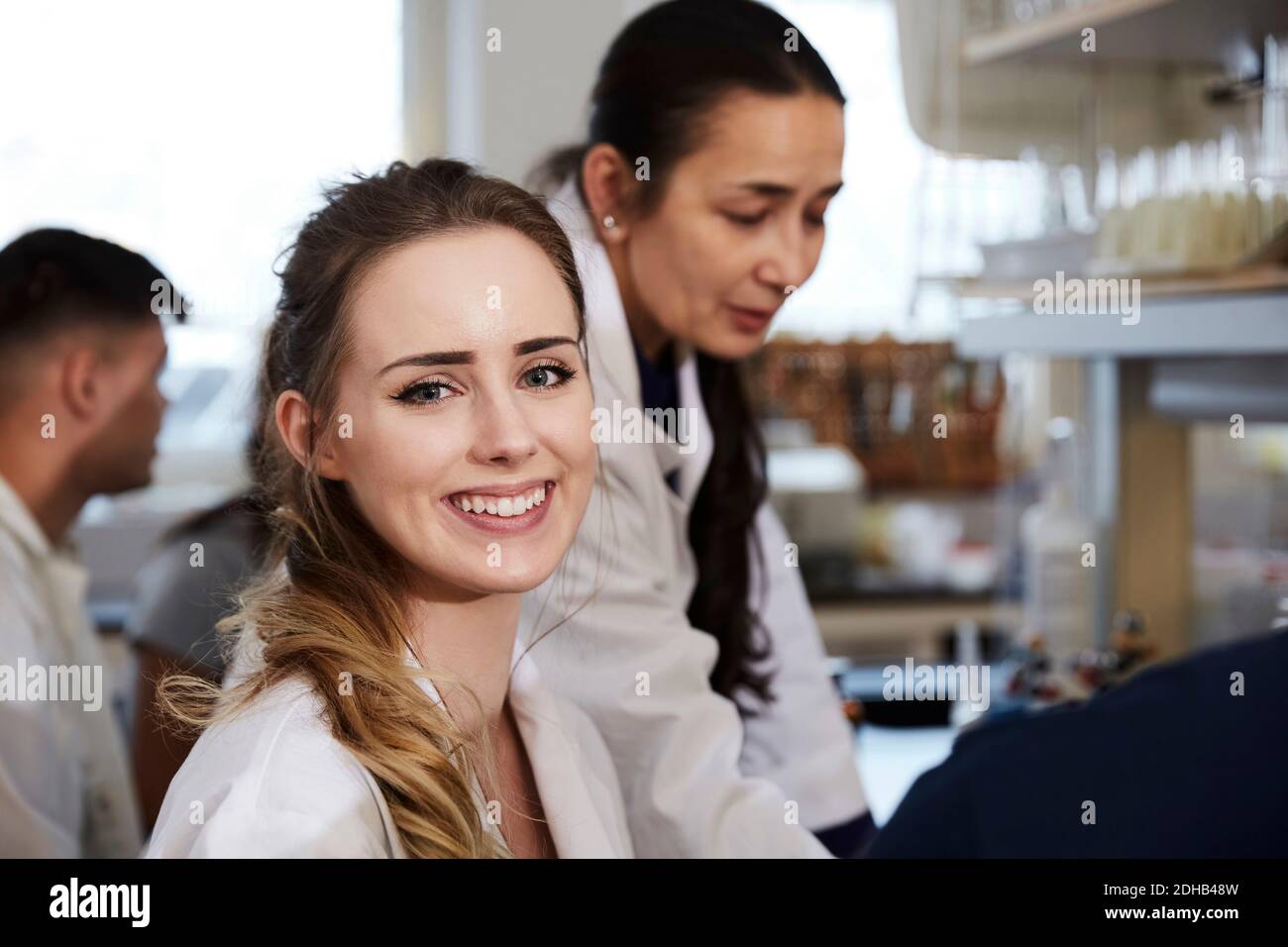 Portrait of smiling young female student sitting against teacher ...