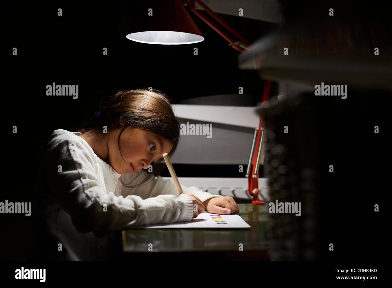 Girl studying while sitting at illuminated desk in darkroom Stock Photo ...