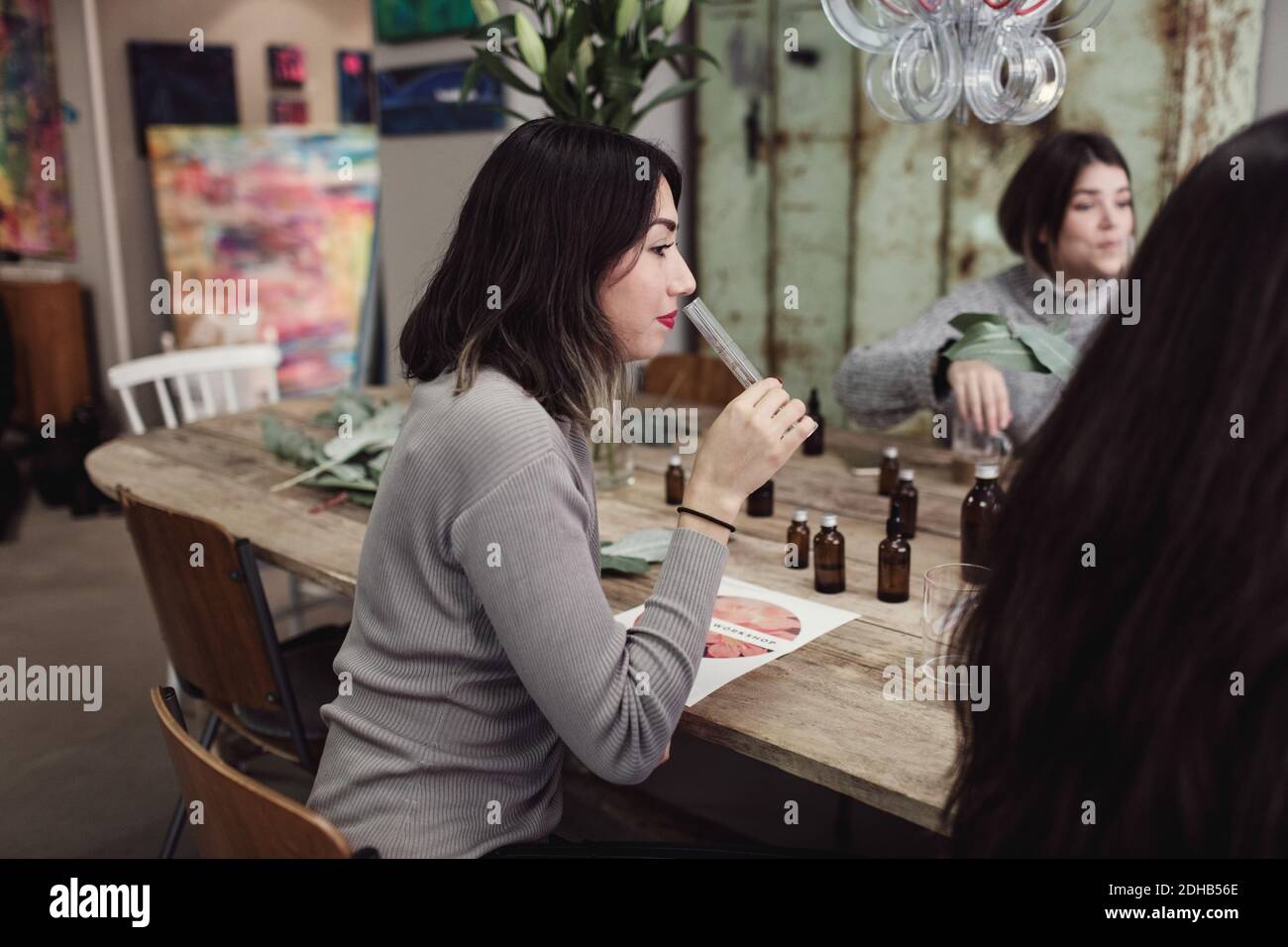 Side view of young woman smelling liquid from test tube while sitting ...