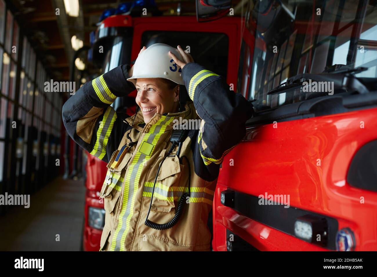 Smiling female firefighter wearing helmet while standing by fire engine ...