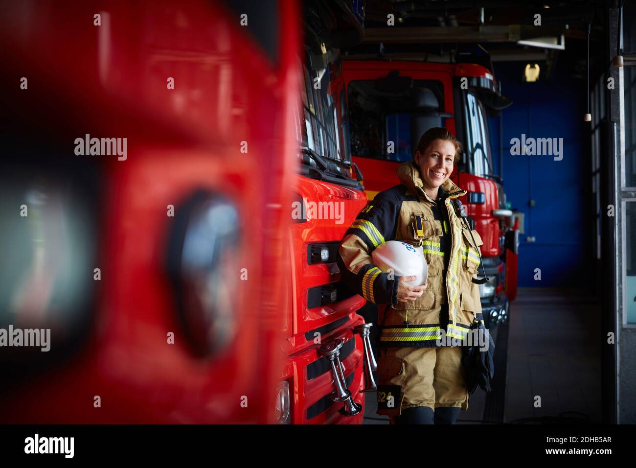 Portrait of smiling firefighter with helmet standing by fire engine at ...