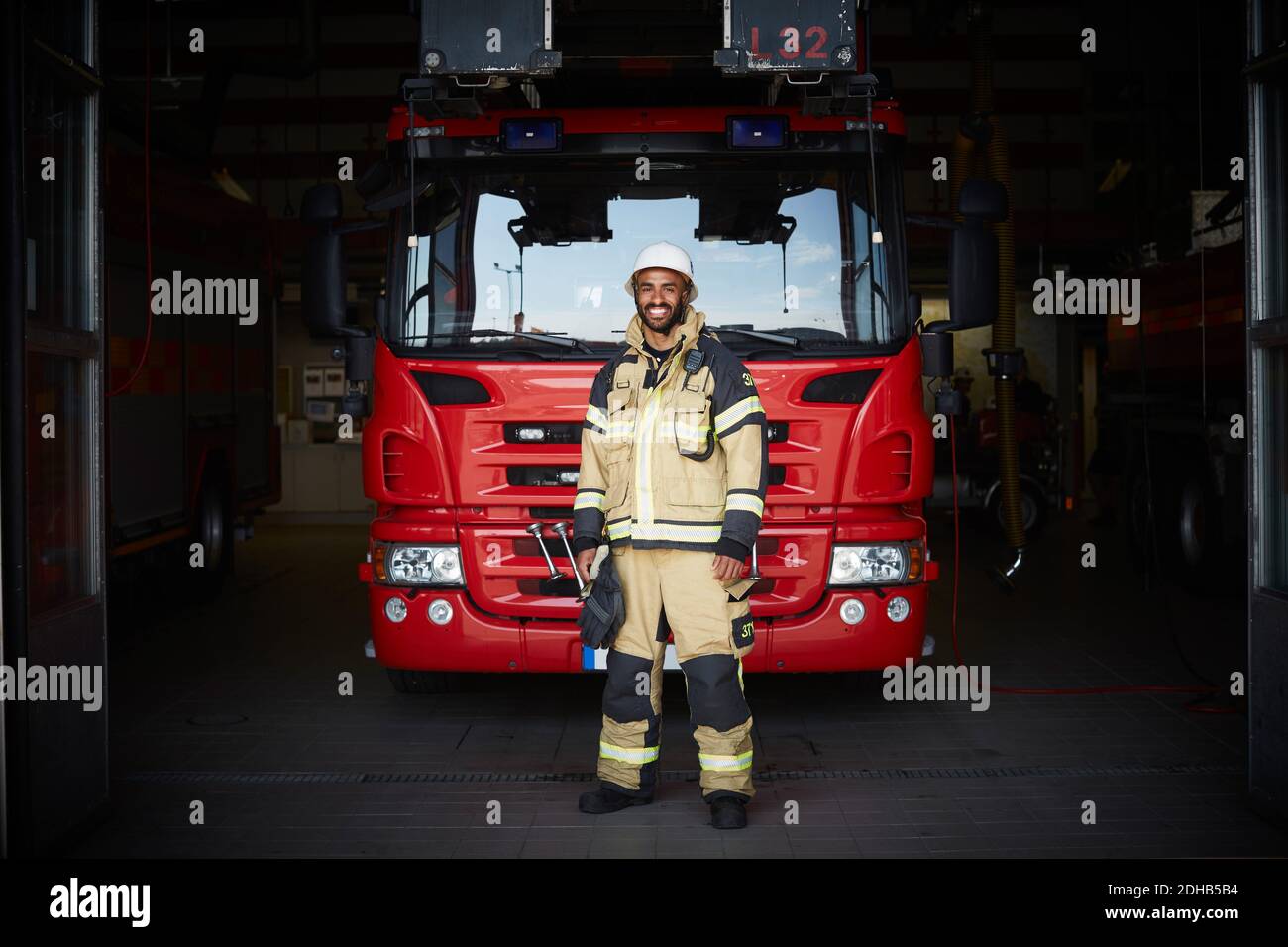 Full length portrait of smiling male firefighter standing in front of ...
