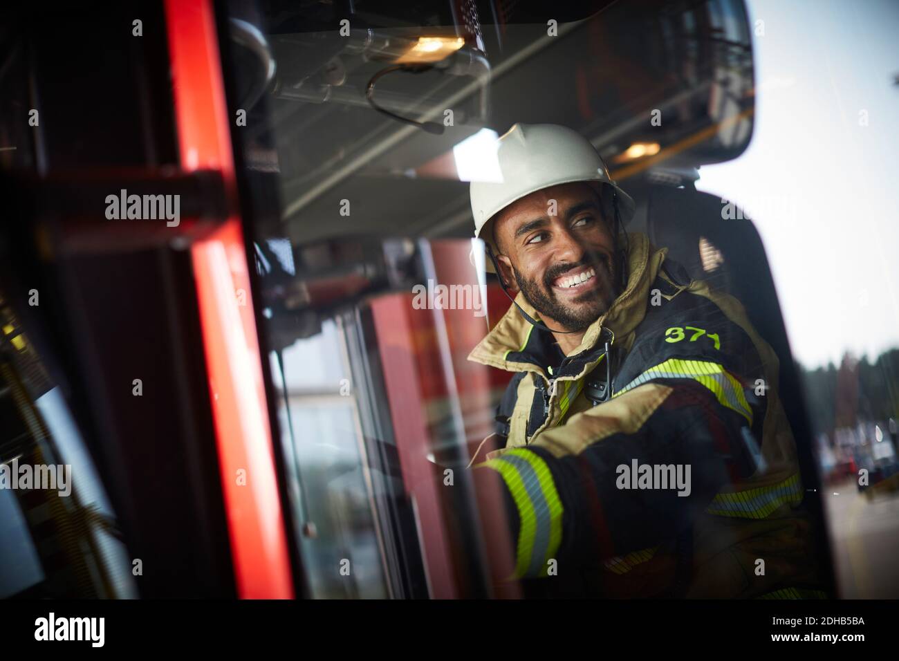 Smiling firefighter sitting in fire engine seen through glass window ...
