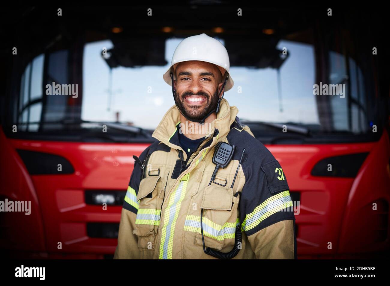 Portrait of smiling firefighter standing in front of fire engine at ...