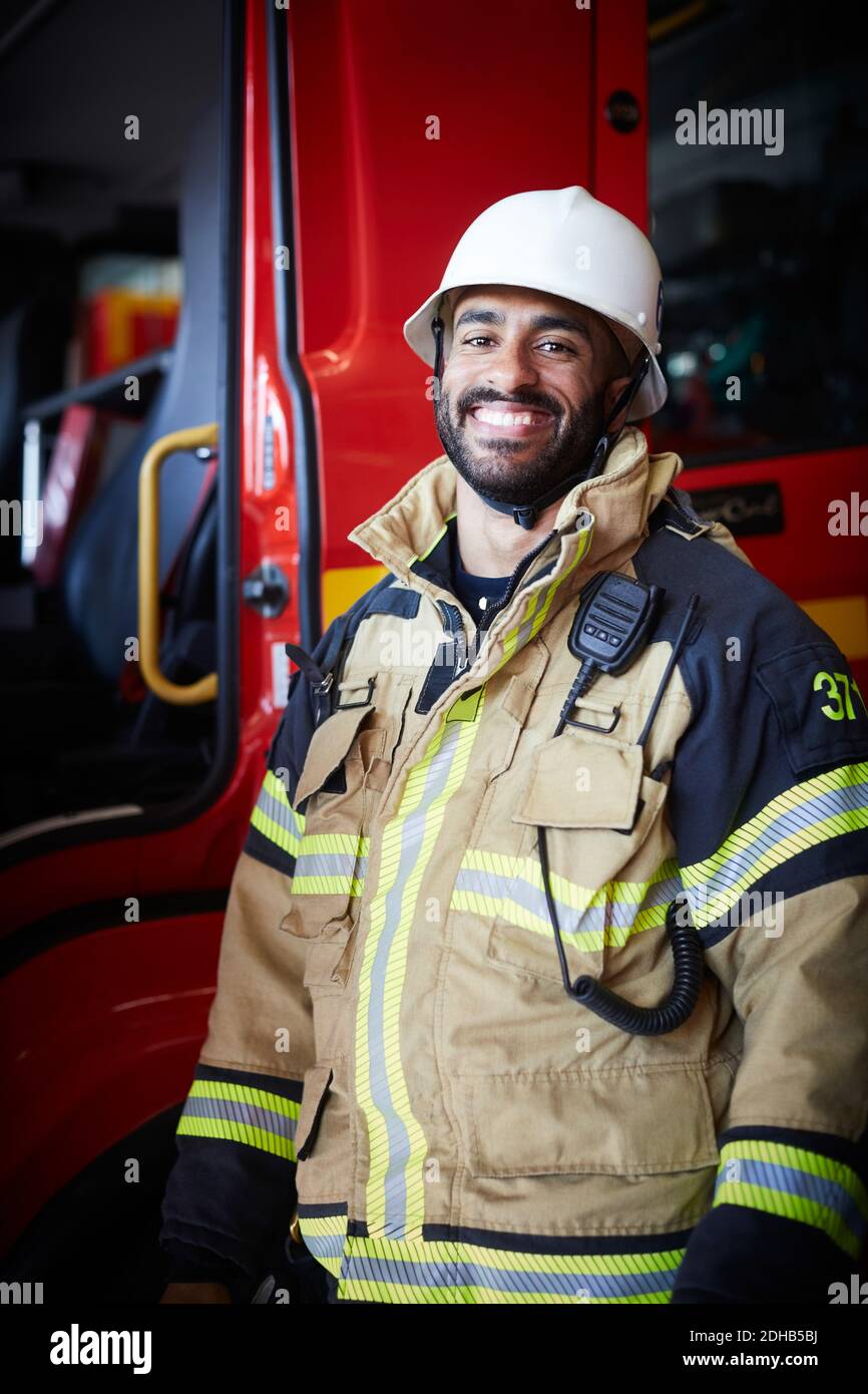Portrait of smiling male firefighter standing against fire engine at ...