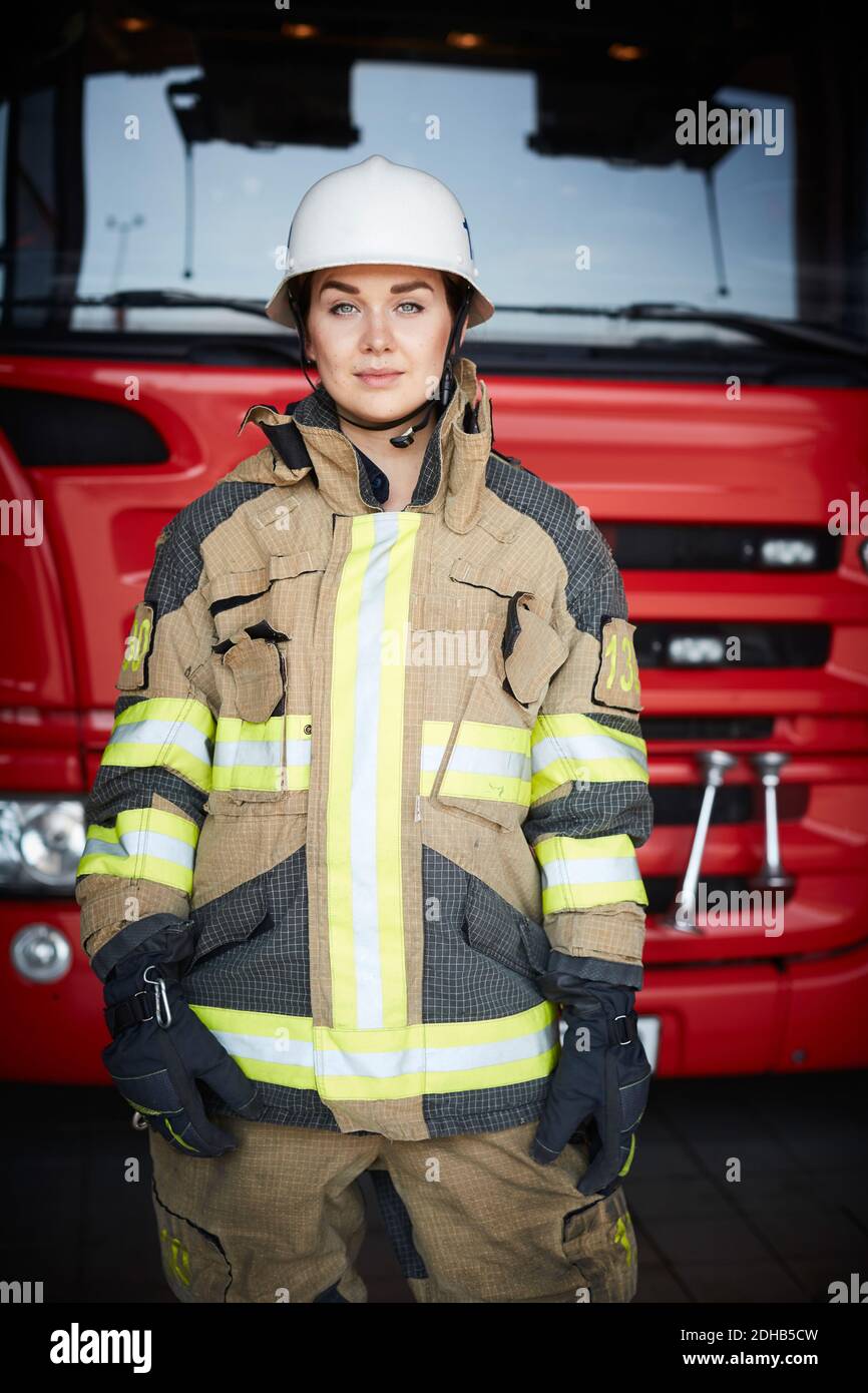 Portrait of confident firefighter standing in front of fire engine at ...