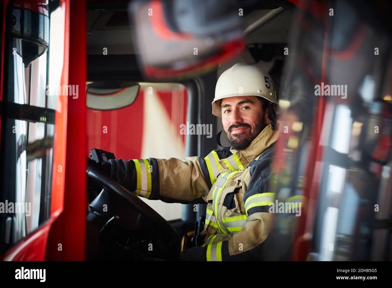 Portrait of confident male firefighter sitting in fire engine at fire ...