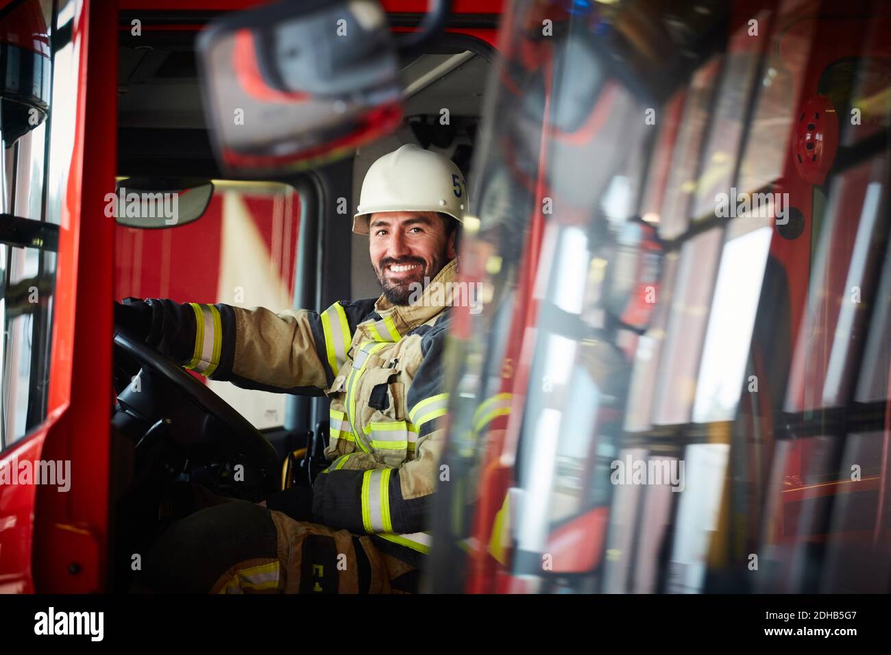 Portrait of mid adult firefighter sitting in fire truck at fire station ...