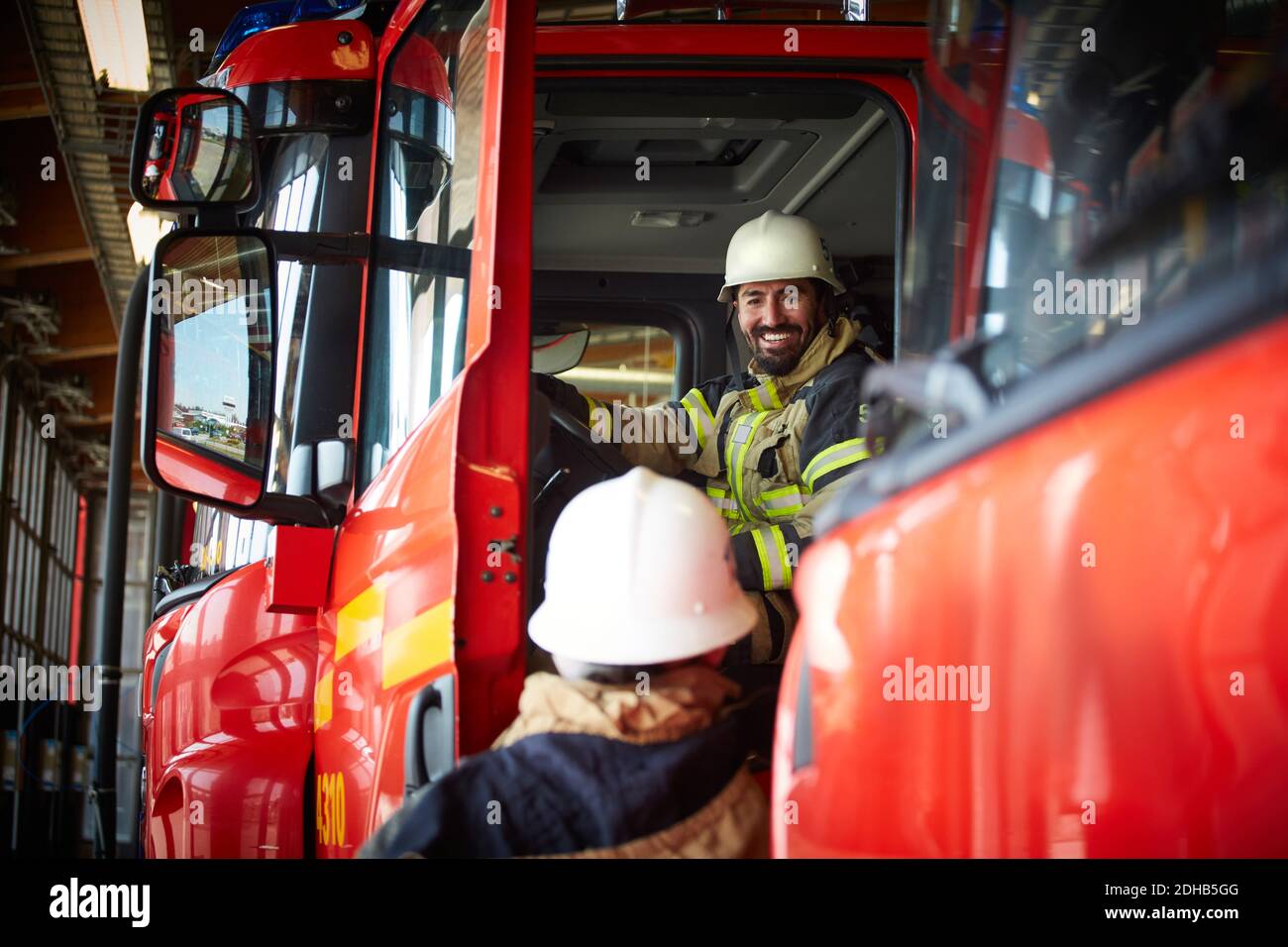 Smiling firefighter talking to coworker while sitting in fire truck at ...