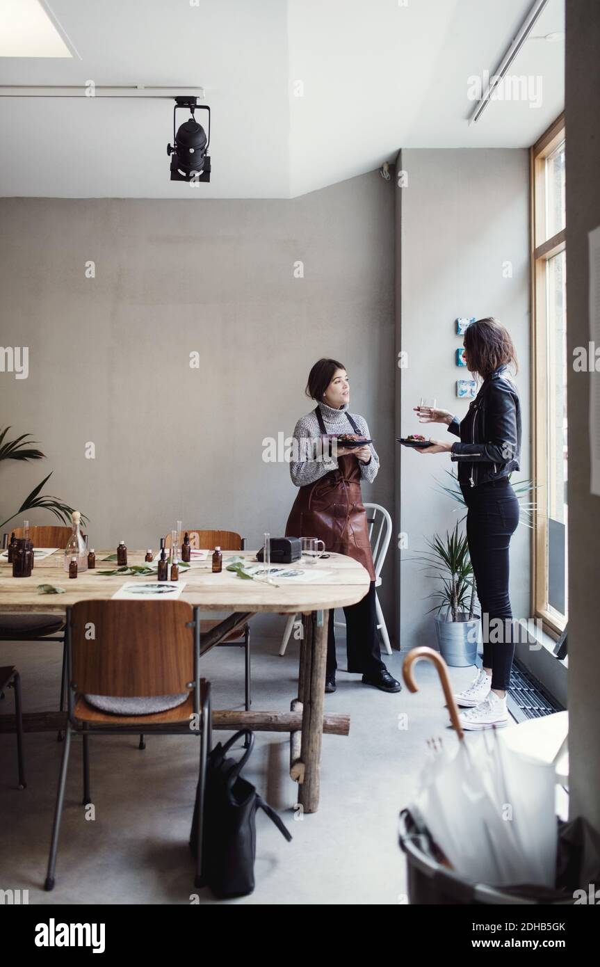 Full length of female colleagues eating lunch at perfume workshop Stock ...