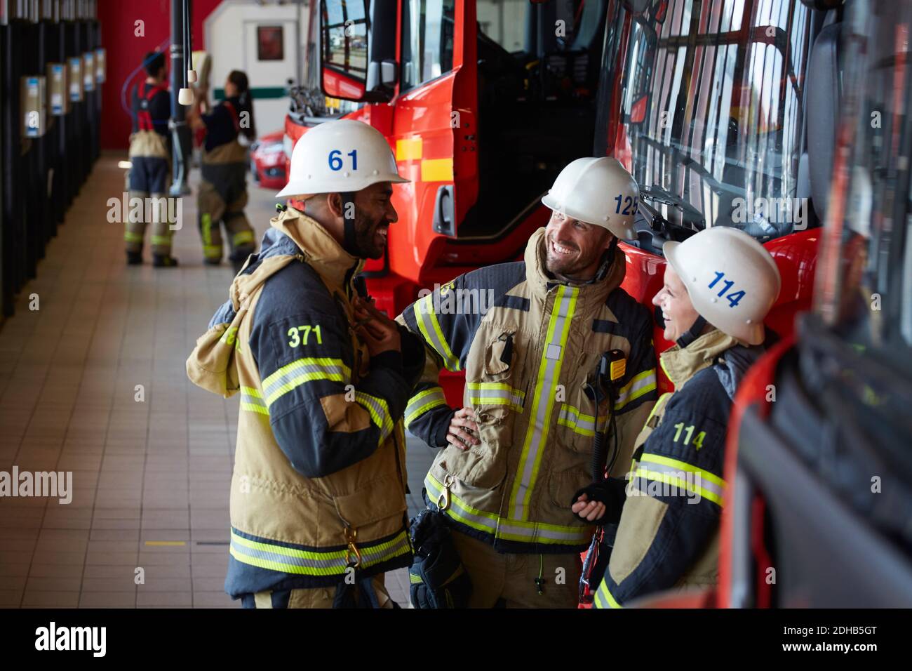 Coworkers smiling while standing against fire engine at fire station ...
