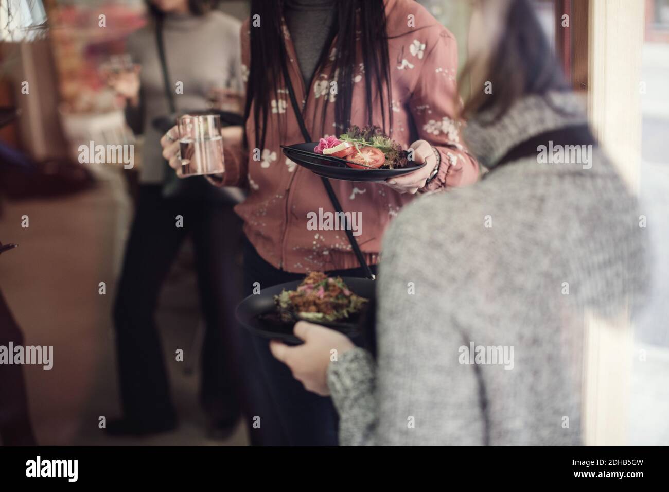 Female colleagues eating lunch while standing at workshop seen from ...