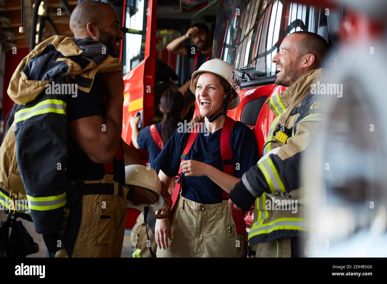 Happy firefighters talking while standing against fire engine at fire ...