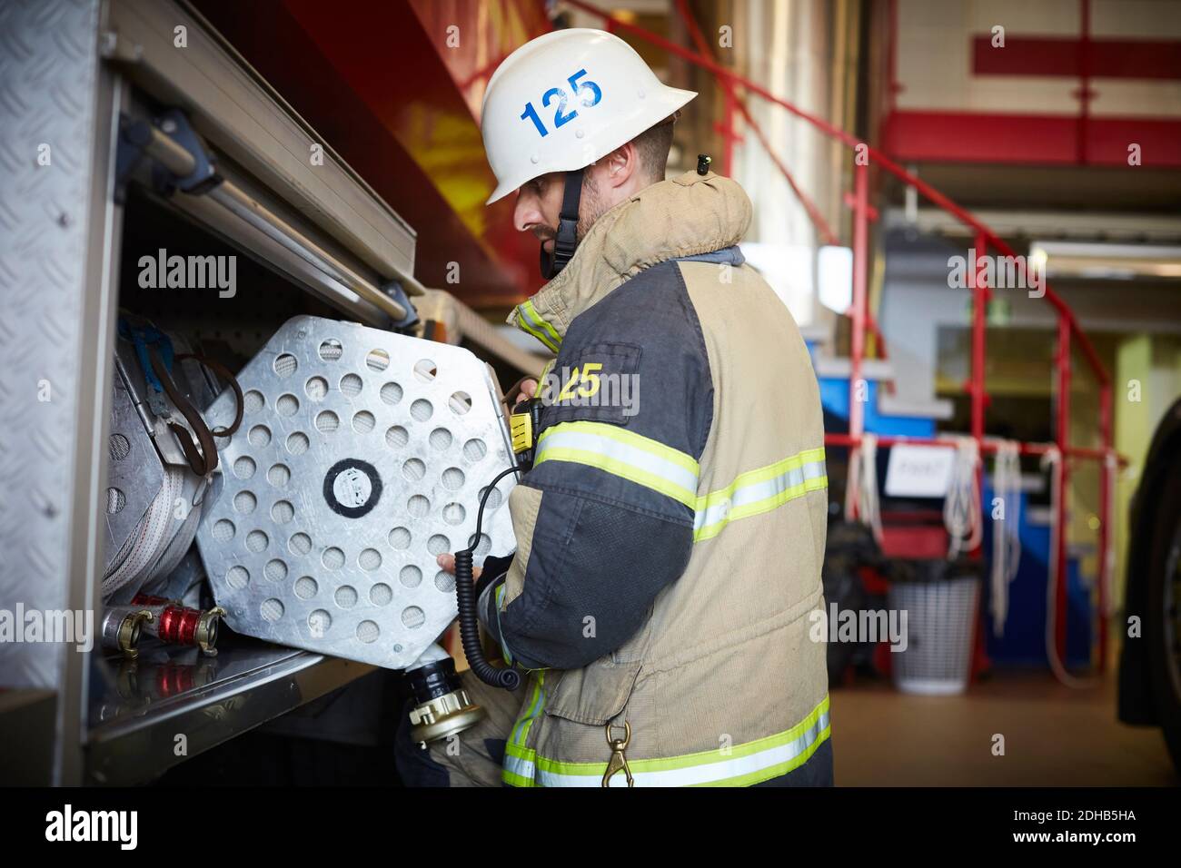 Side view of firefighter arranging fire hose in fire engine at station ...