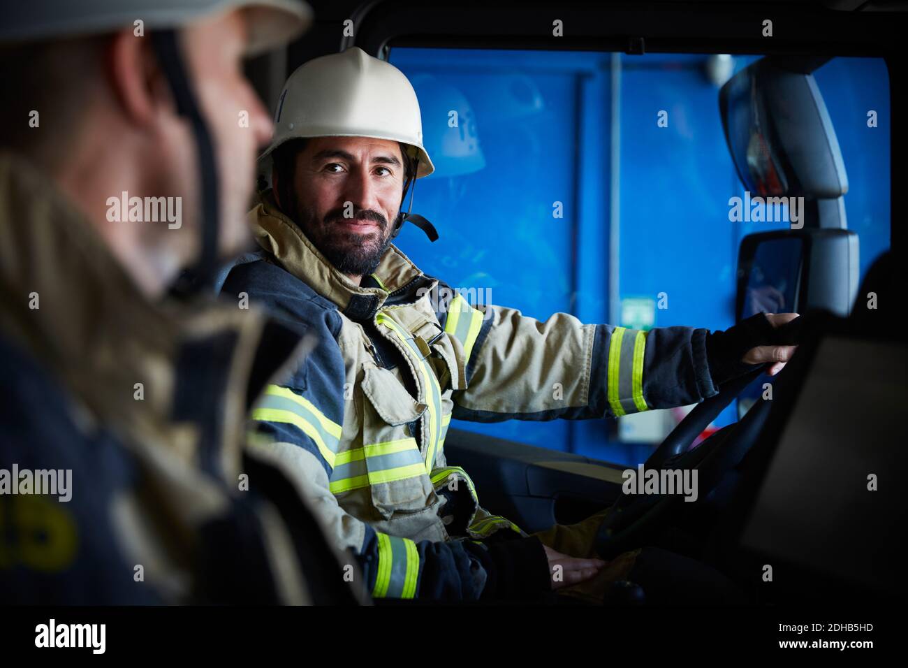 Firefighter looking at coworker while sitting in fire truck Stock Photo ...