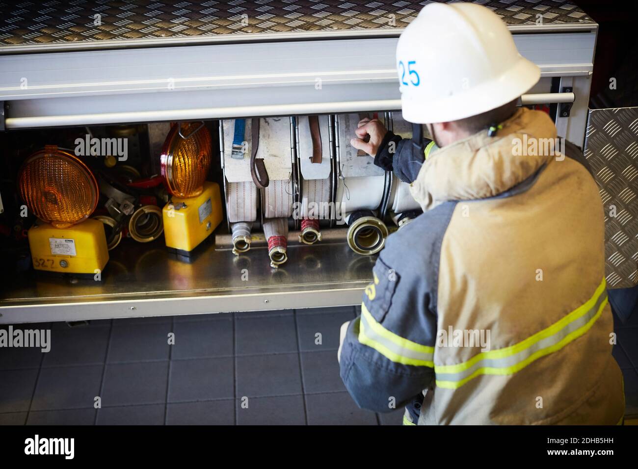 Rear view of firefighter arranging fire hose in engine at fire station ...