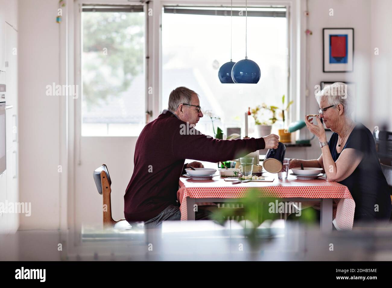 Side view of senior couple eating food at dining table against window ...