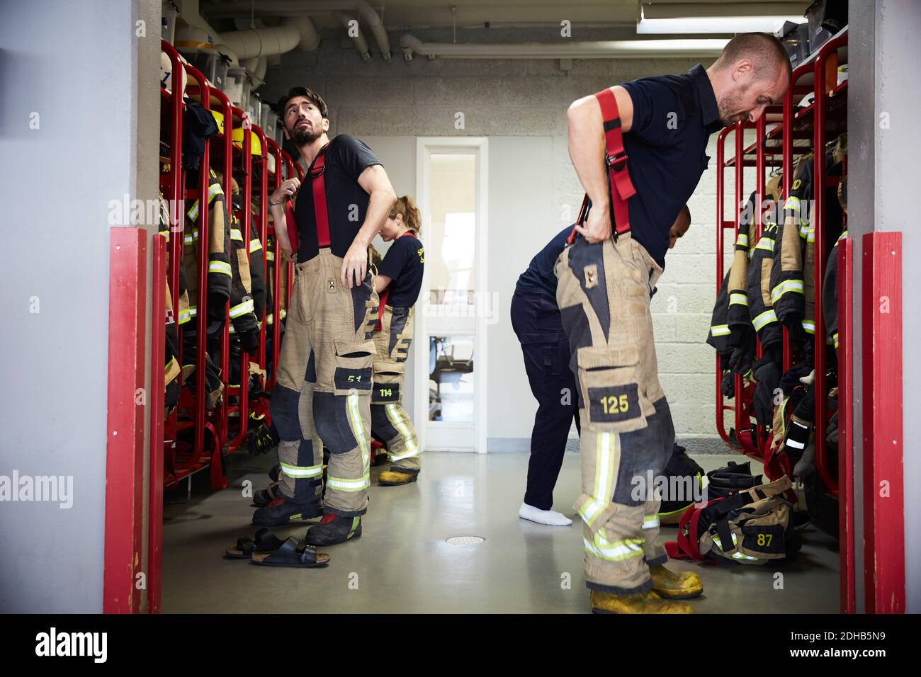 Firefighters wearing protective workwear in locker room at fire station ...