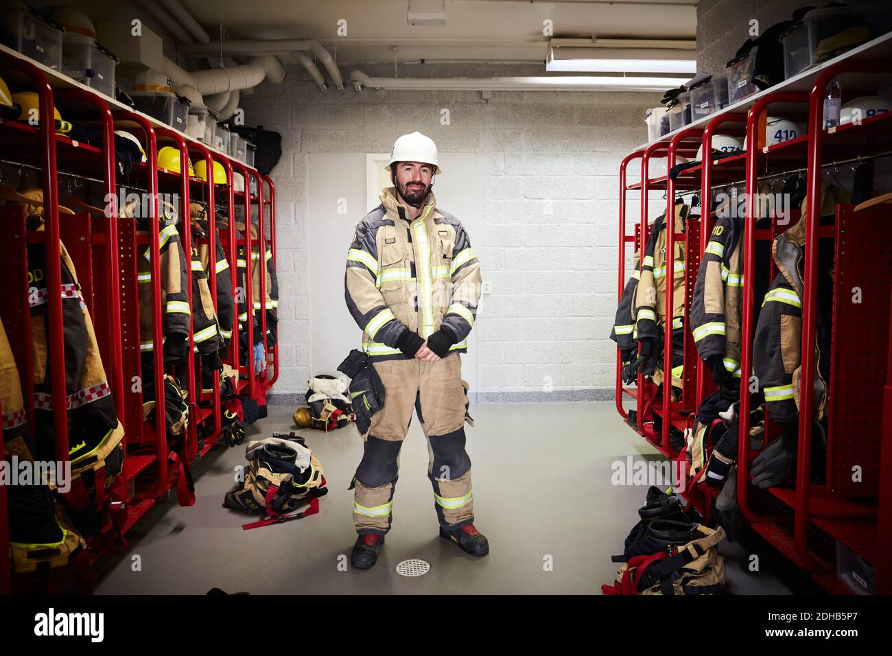 Full length of male firefighter standing in locker room at fire station ...