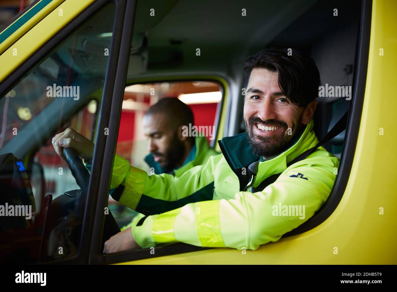 Portrait of smiling male paramedic with coworker driving ambulance in ...