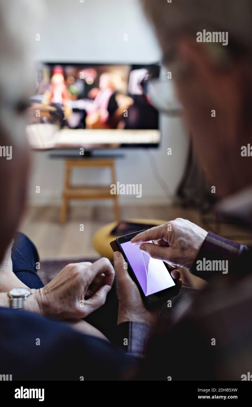 Senior couple sitting with mobile phone watching TV at home Stock Photo ...