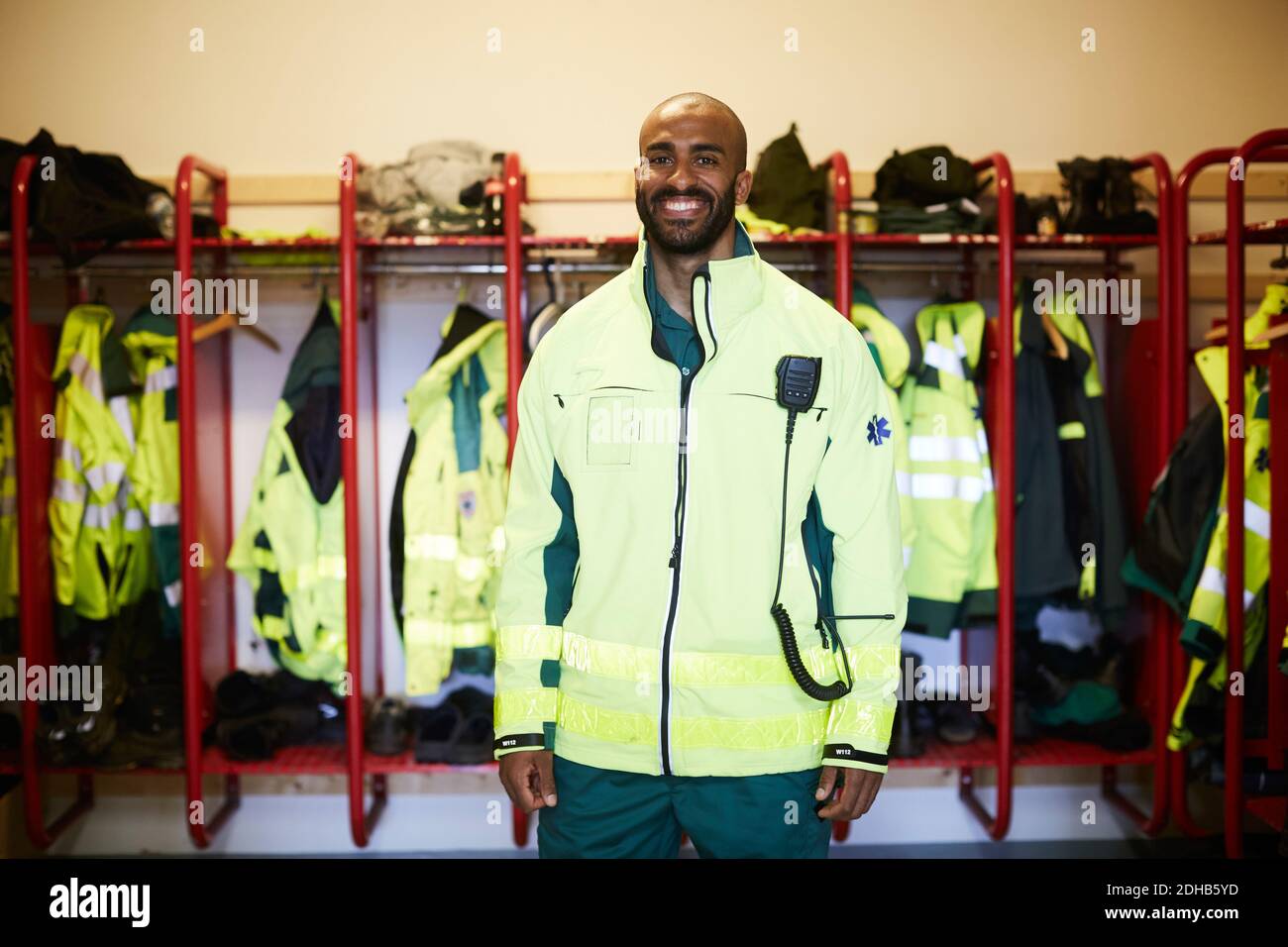 Portrait of smiling mid adult paramedic standing in locker room at ...
