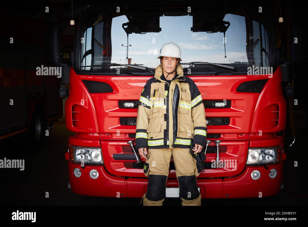 Portrait of female firefighter standing in front of fire engine at fire ...