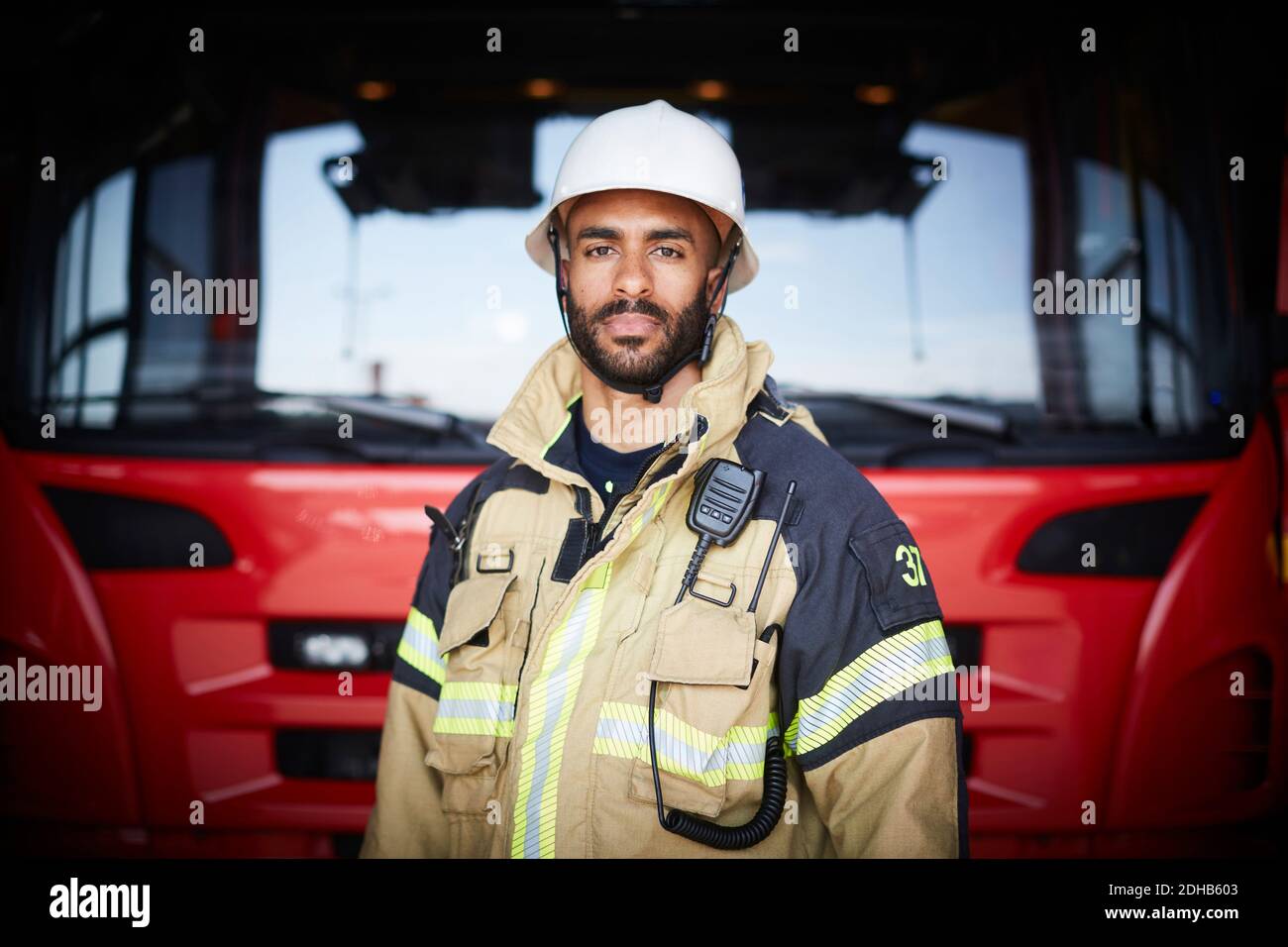 Portrait of confident firefighter standing in front of fire engine at ...