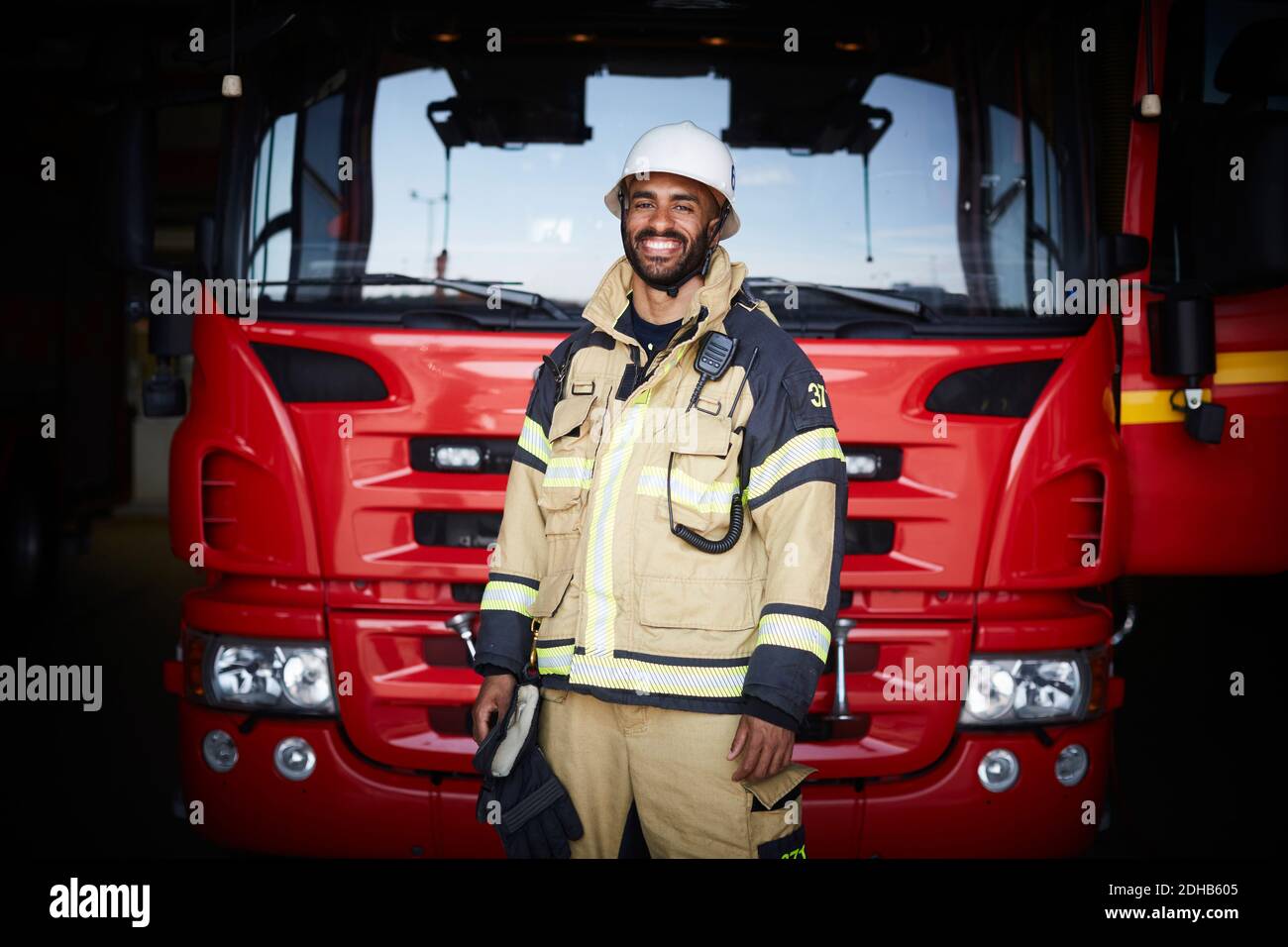 Portrait of smiling firefighter in uniform standing against fire engine ...