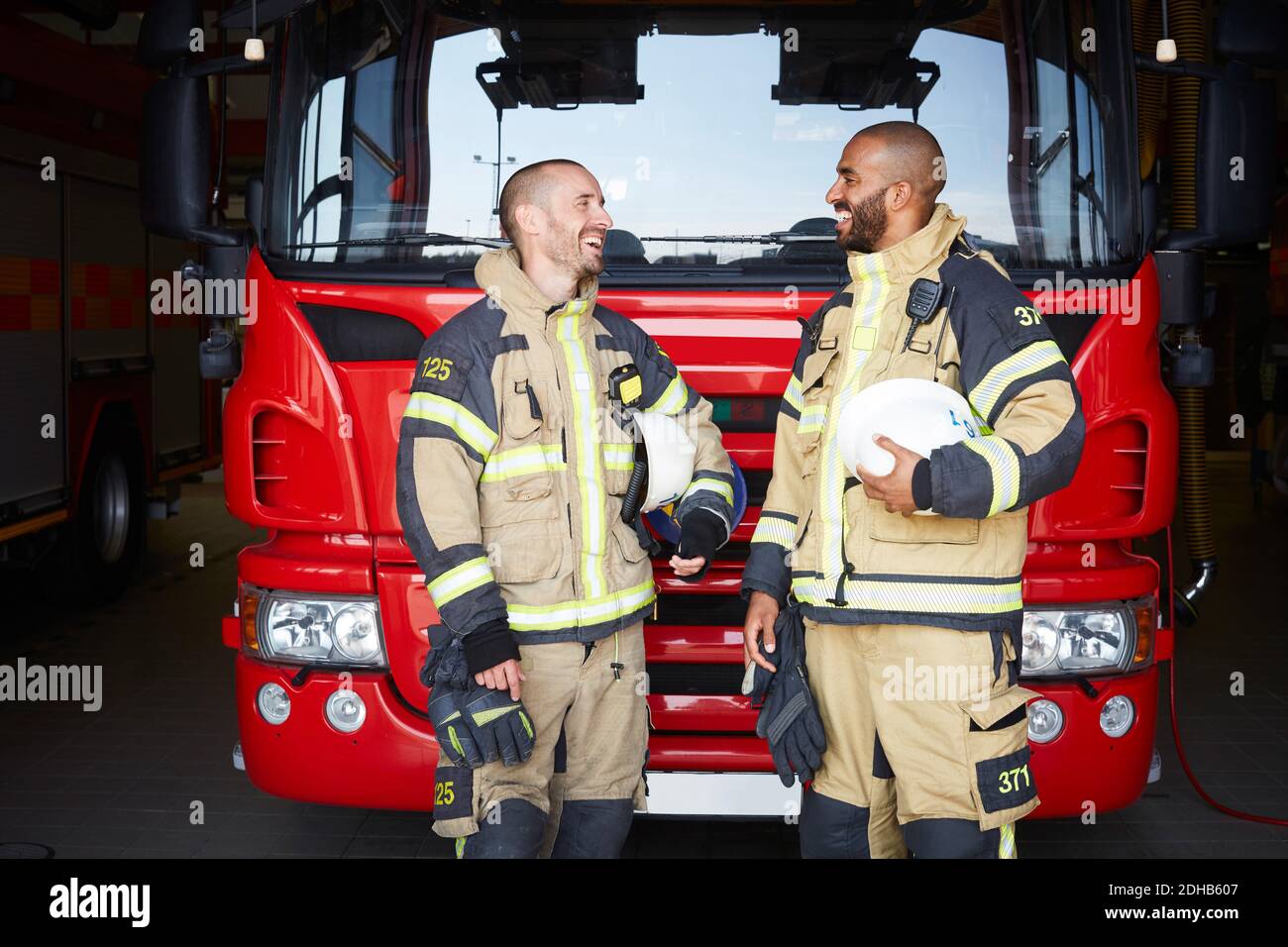 Happy firefighters talking while standing in front of fire engine at ...