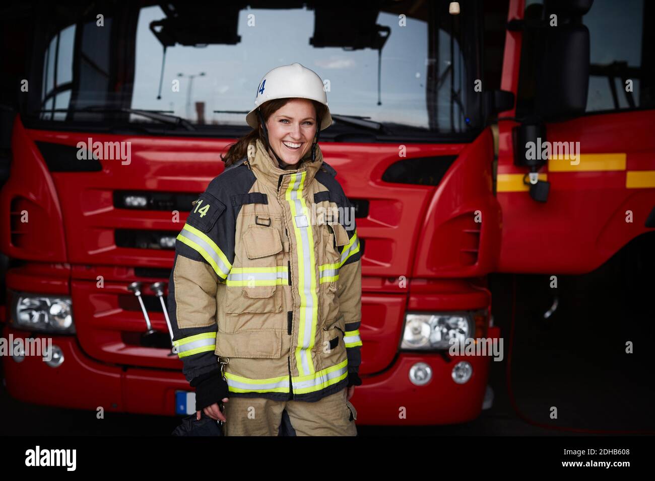 Portrait of smiling female firefighter standing in front of fire engine ...