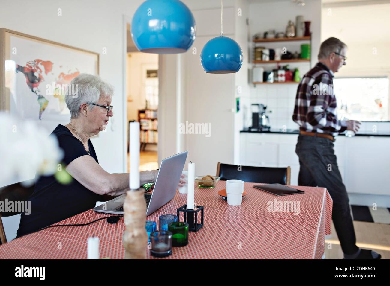 Side view of senior woman sitting with laptop at dining table while man ...