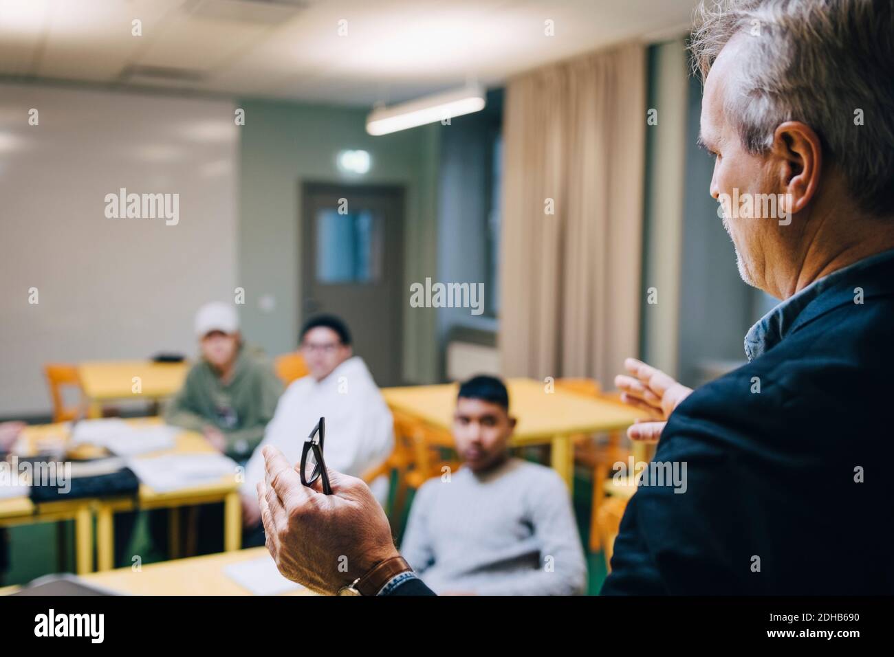 Male teacher gesturing while teaching students in classroom Stock Photo ...