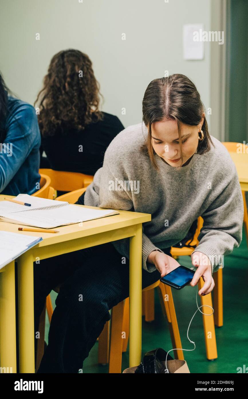 Teenage girl using smart phone while sitting at desk in classroom Stock ...