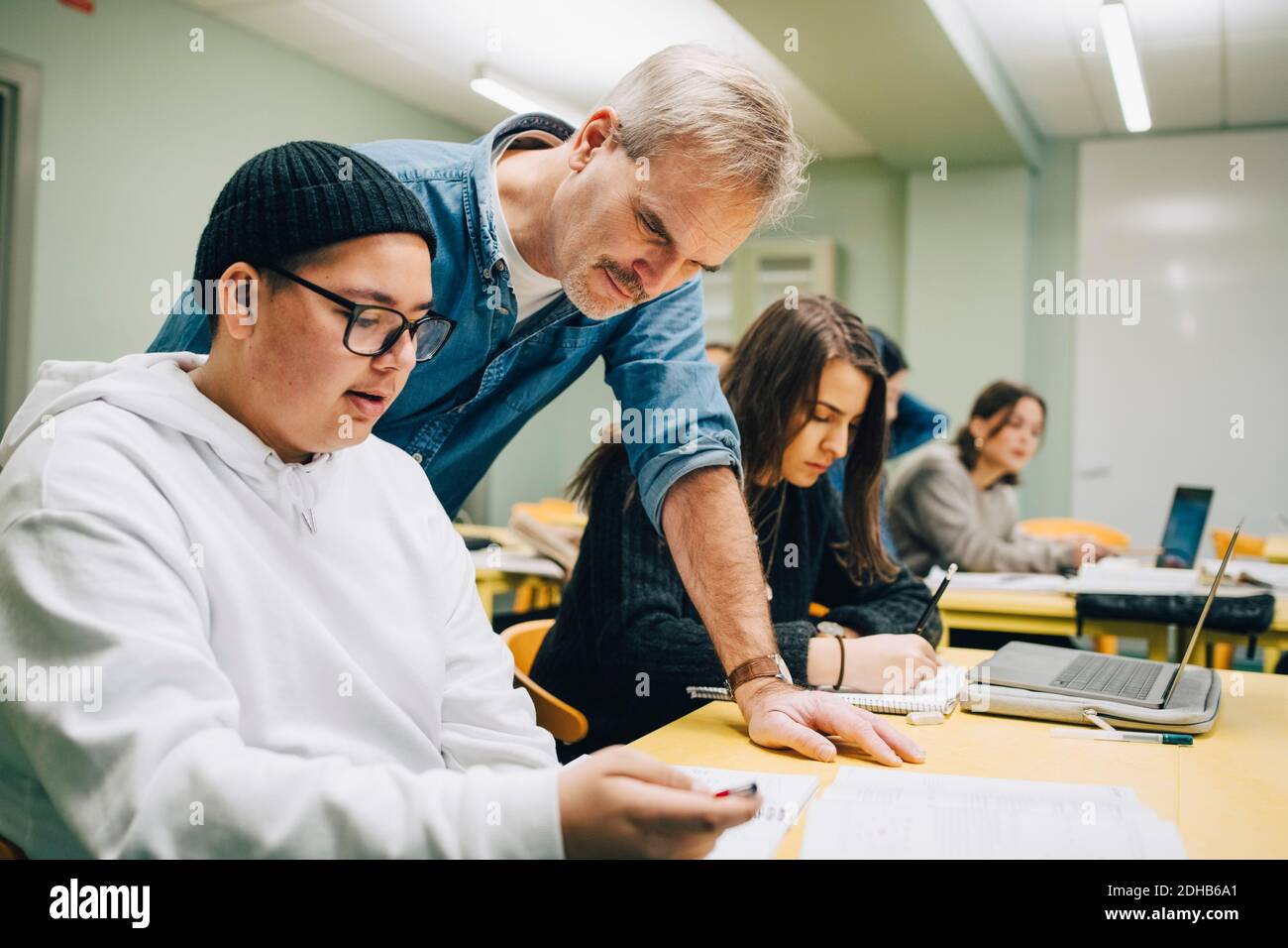 Male teacher assisting student at desk in classroom Stock Photo - Alamy