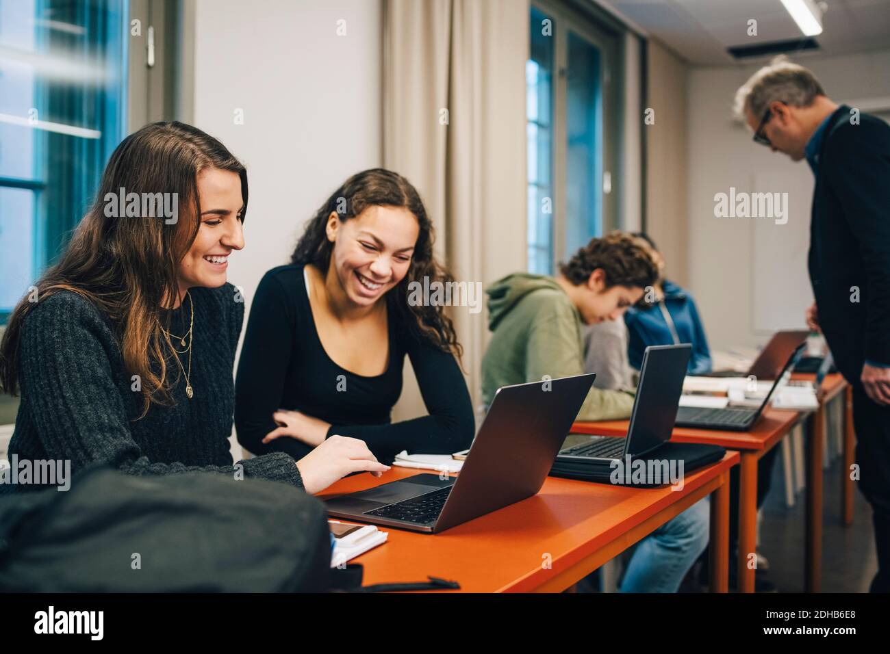 Cheerful female high school students using laptop at desk in classroom ...