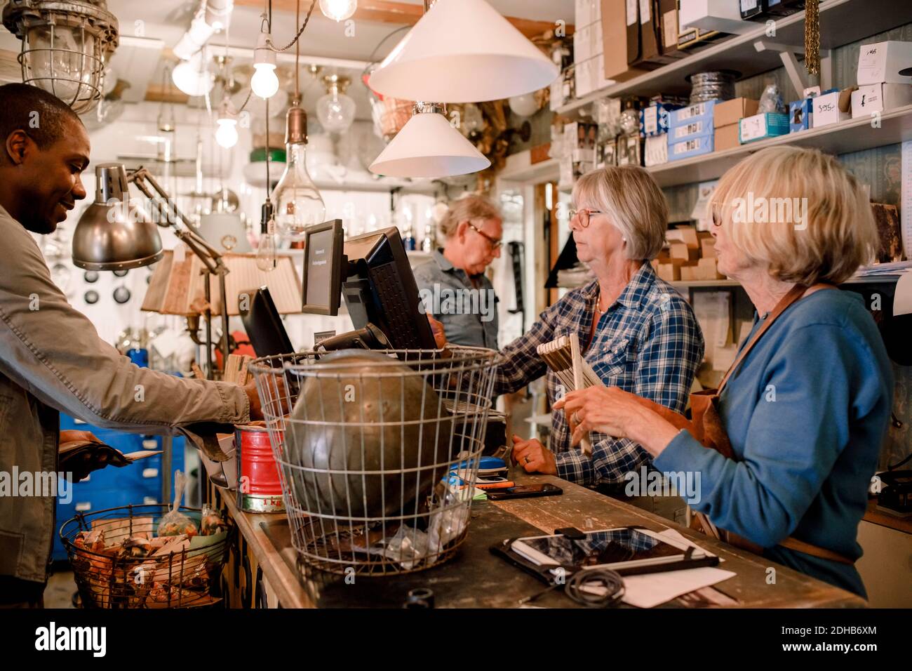 Male customer standing with female owners at checkout in hardware store ...